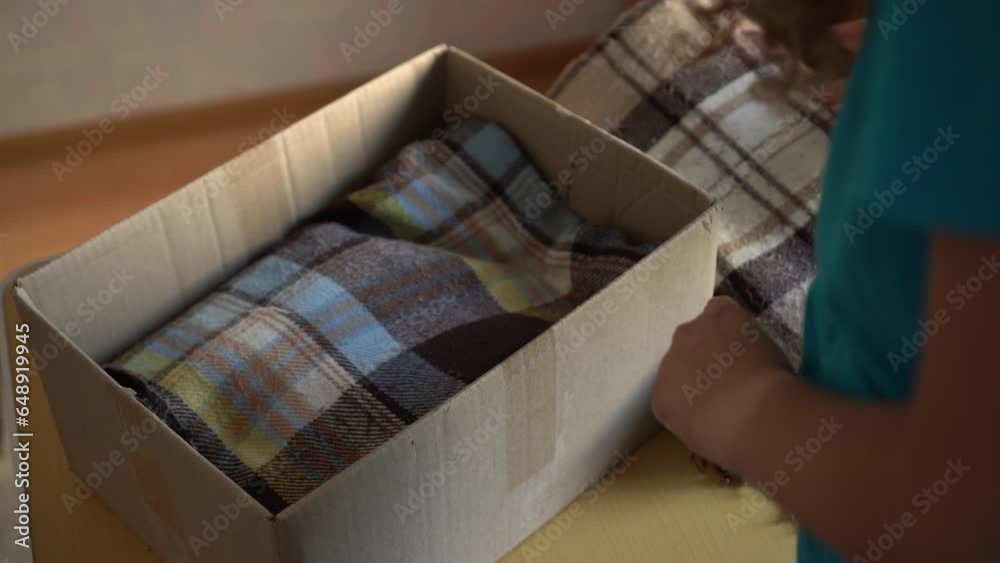 Volunteer stacking warm plaid blankets in a donation box. Woman donates ...