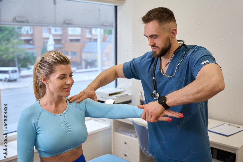 Male traumatologist checking muscle strength and coordination of female ...
