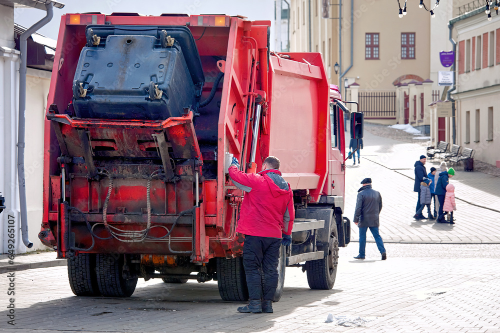 Refuse collector man unload dustbin in rear load garbage truck. Trash ...
