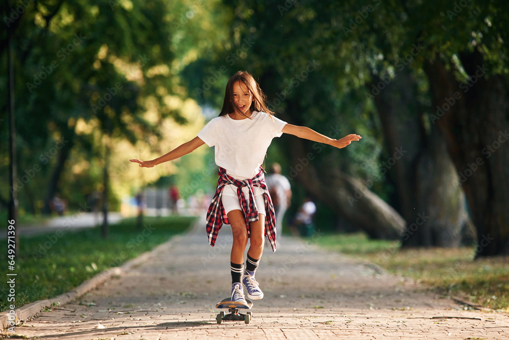 Controlling the balance. Happy little girl with skateboard outdoors ...