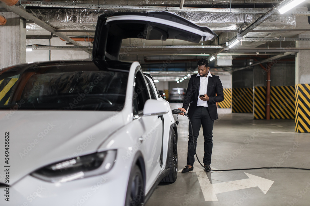 Attractive african american man inserting charger gun in EV port while ... Attractive african american man inserting charger gun in EV port while ...