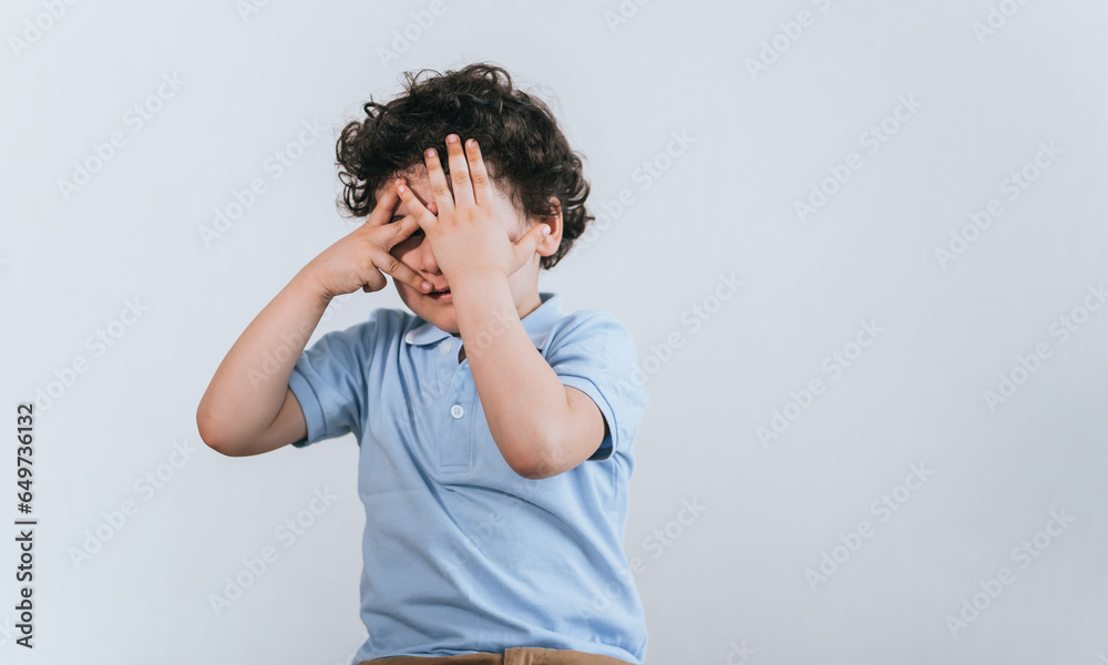 Little curly boy in casual hiding face by palms, feels fear stands ...
