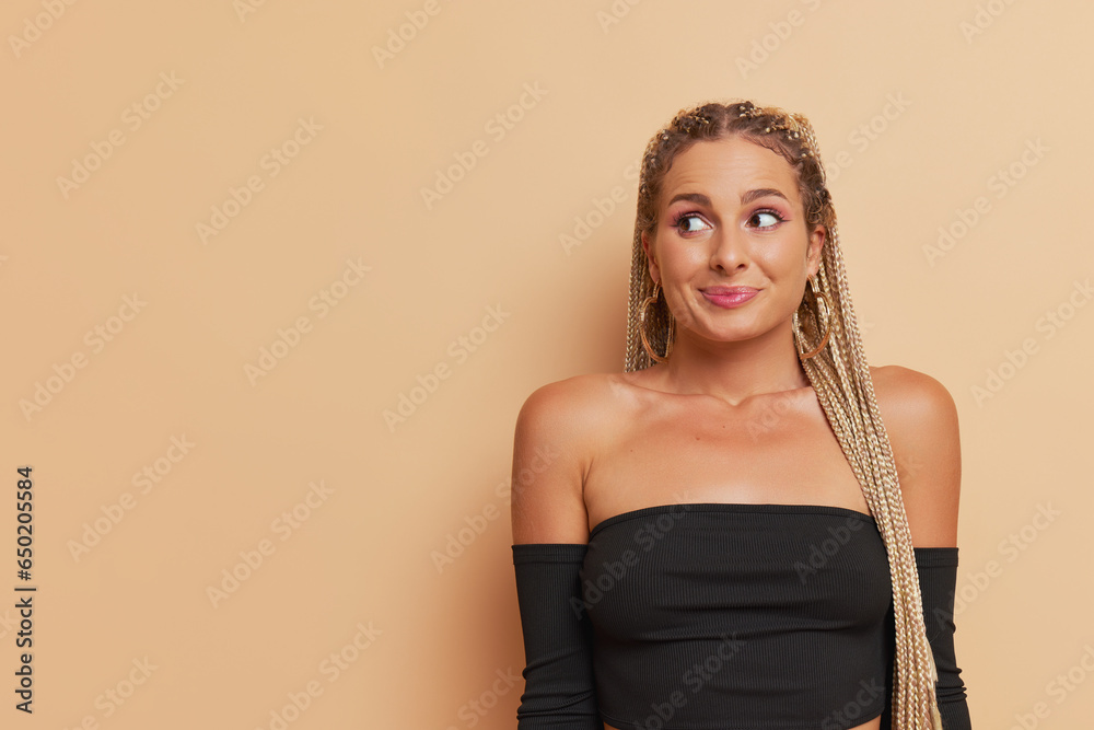 Pretty woman in black bare shoulder top standing aside on light brown ...