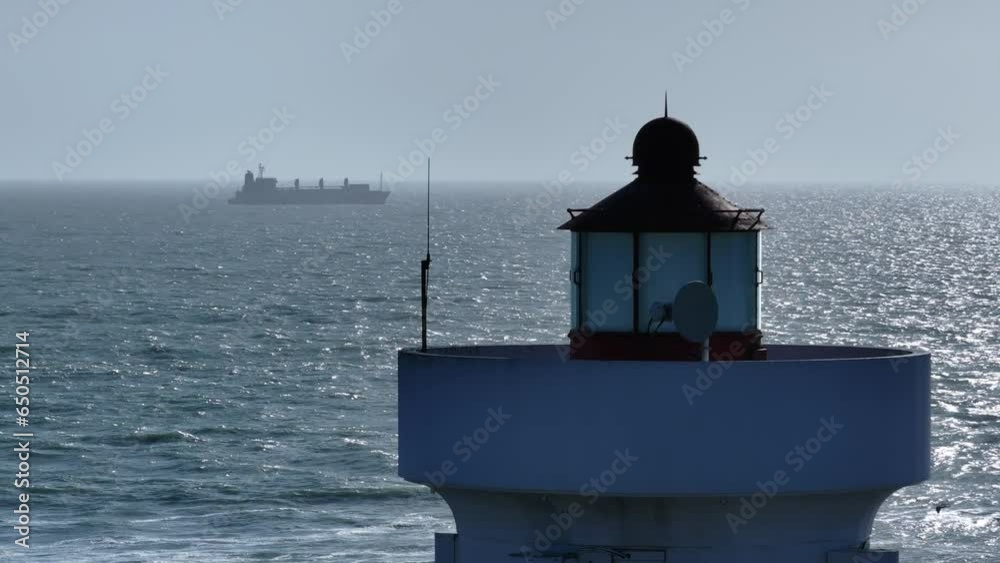 Zoomed-in aerial view of a lighthouse in foreground with cargo vessel ...