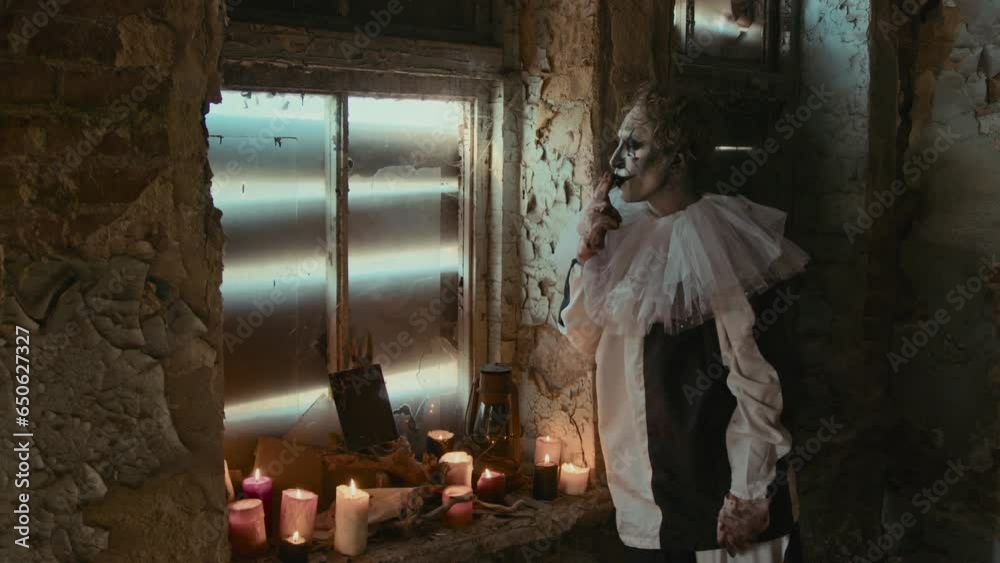 Zoom in shot of man in costume of clown smoking cigarette standing next ...