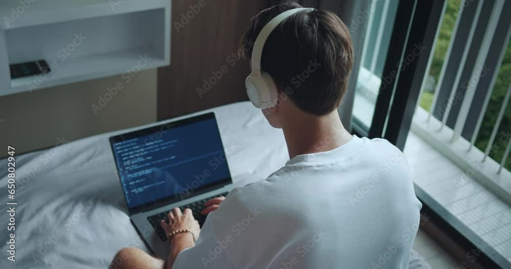 Rear view man freelancer programmer in headphones sitting on bed in ...