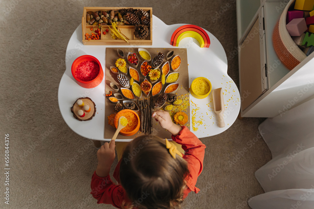 A little girl playing with autumn natural materials and make a tree ...