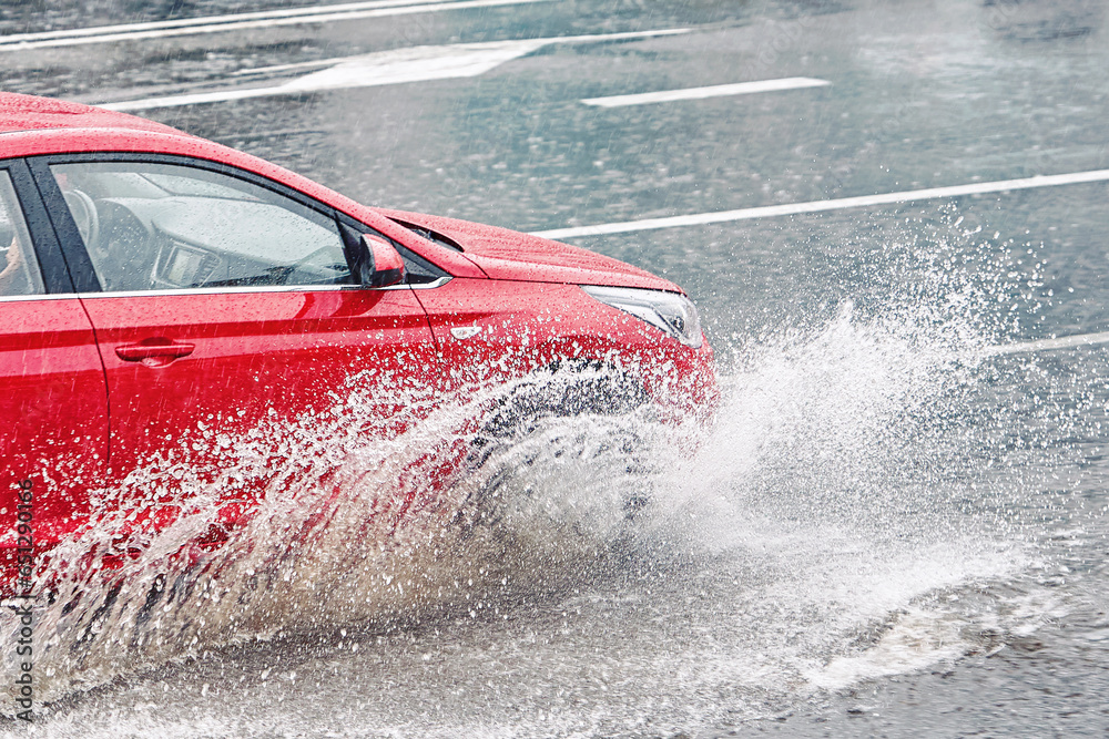 Red car driving through puddle during heavy rain, mooving fast on wet ...