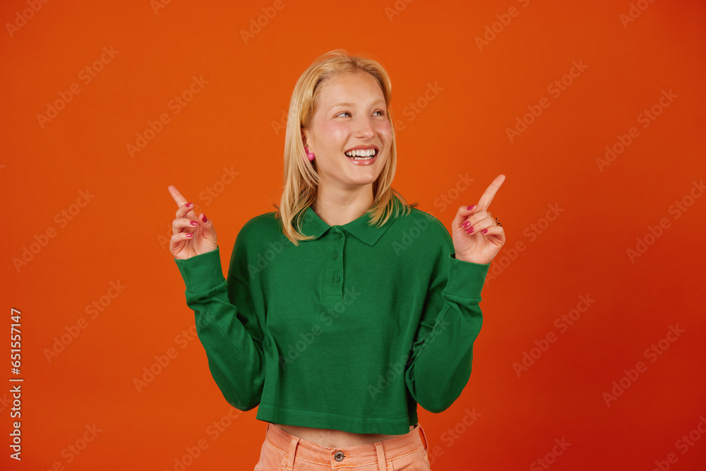 Beautiful young woman raising index fingers in eureka gesture on orange ...