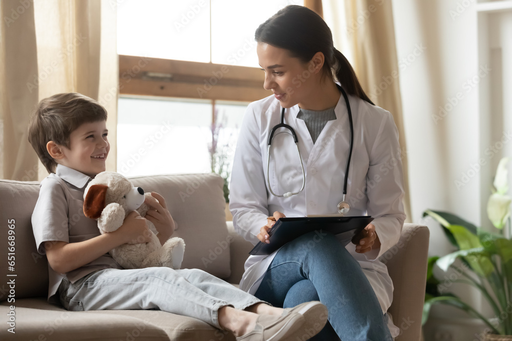 Caring female pediatrician consulting pretty little boy, making notes ...