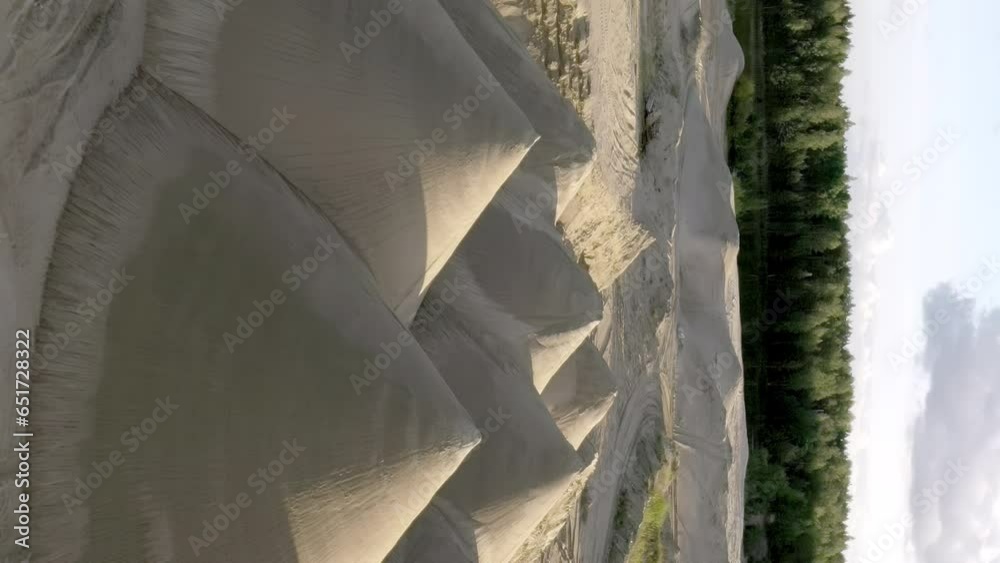 Light-colored sand piles in a mining area. Evening sunshine casts long ...