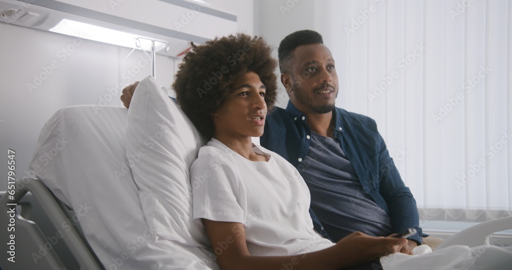 Happy African American teenager rests in hospital room and watches ...