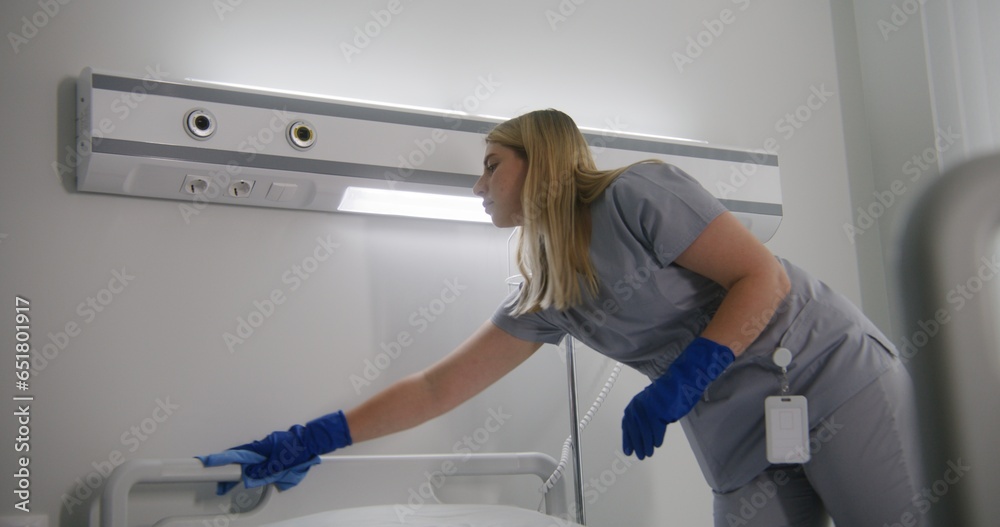 Adult cleaner wipes patient bedside panel and bedside table with rug in ...