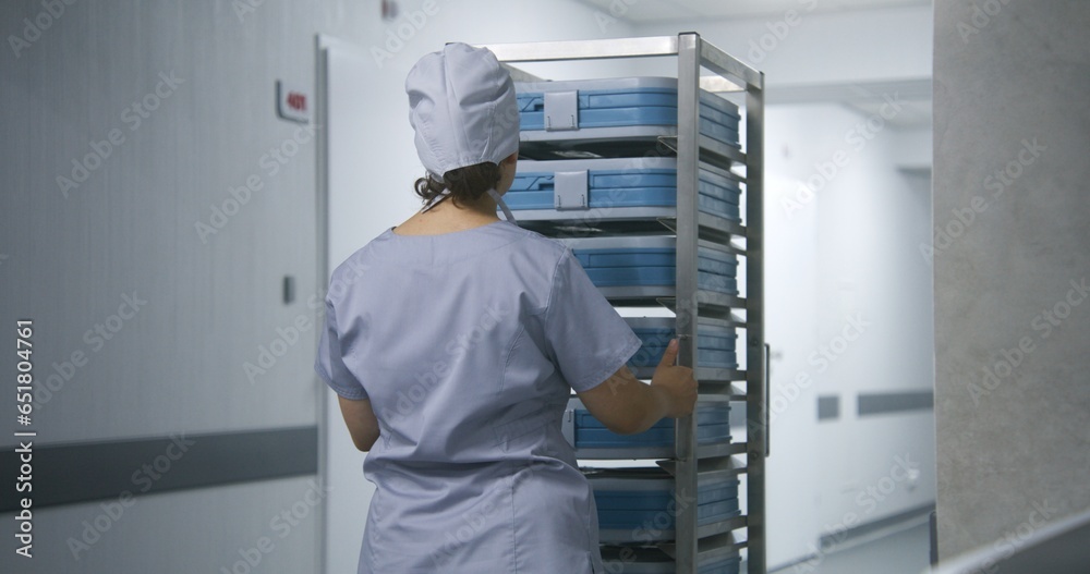 Nurse in uniform pushes mobile shelves with inventory through bright ...