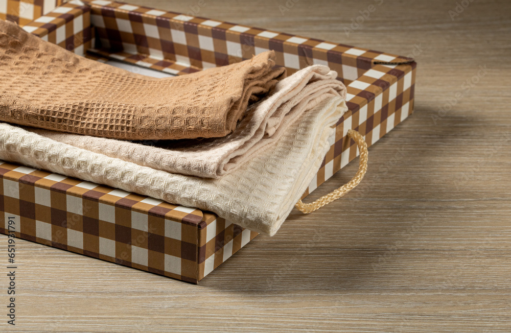 Waffle towels are stacked in a checkered gift box on a wooden table ...
