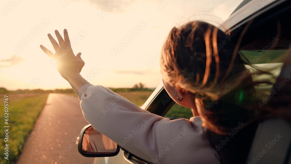Girl with long hair sits in front seat of car, her hand out window and ...