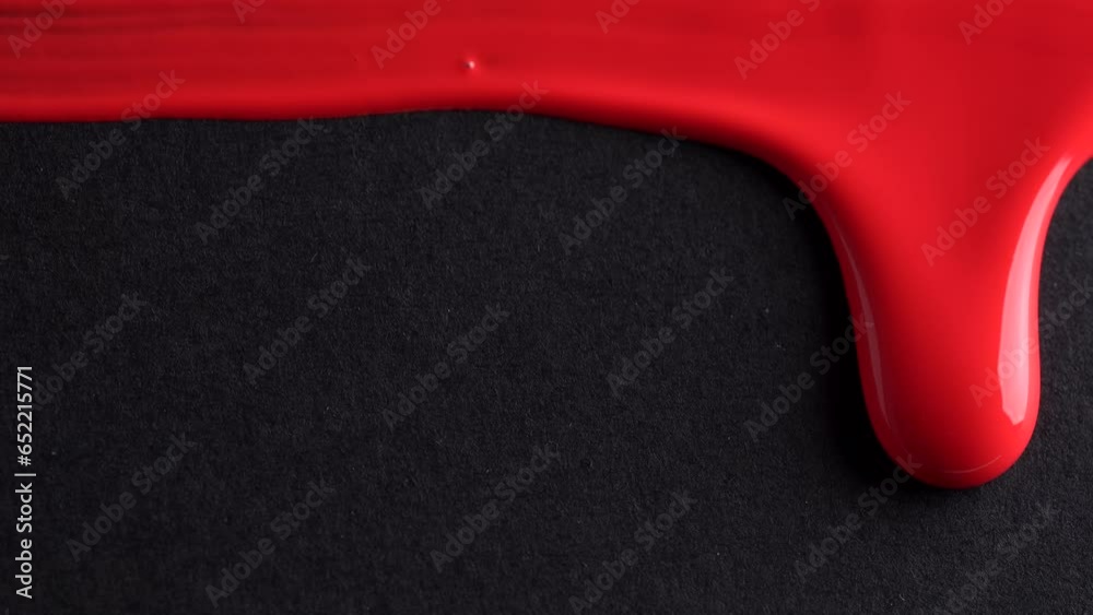 Liquid drops of red paint color flowing on the black surface. Macro ...
