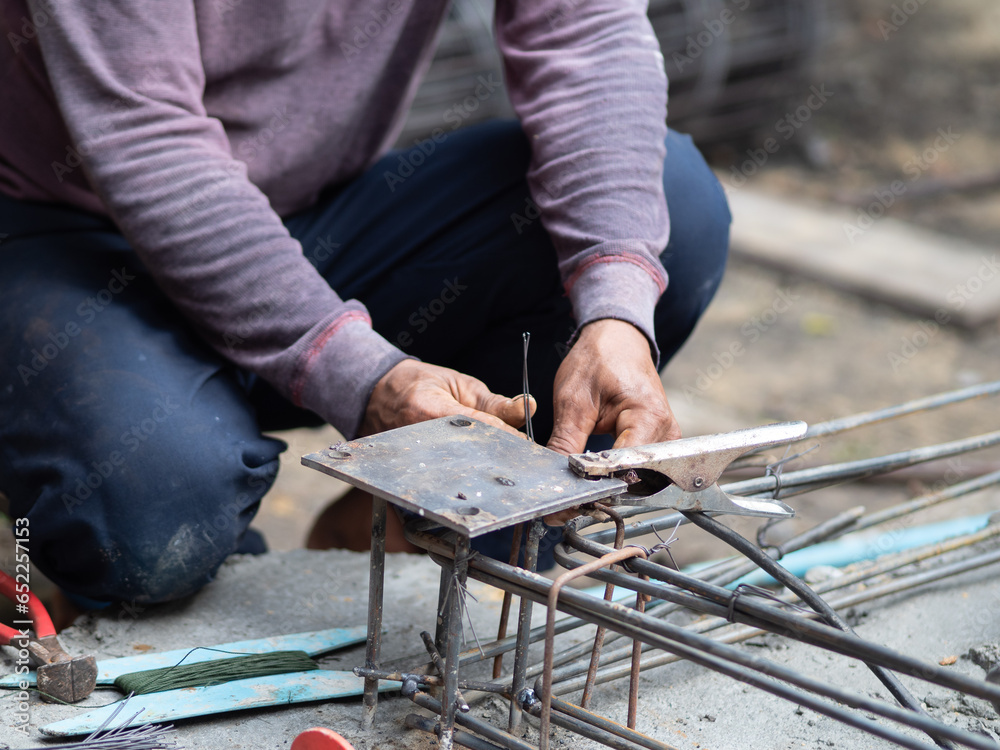 Labor constructor ties steel wire to secure bars rod for reinforcement ...