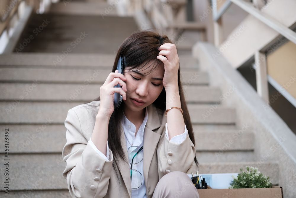 Sad female office worker sitting on stairs of building, talking on her ...