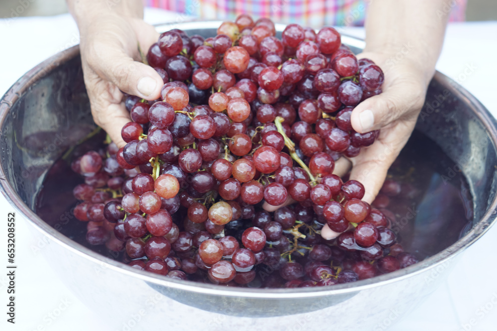 Closeup woman hands is washing grape fruits in sink. Soak fruits in water which mixed with ...