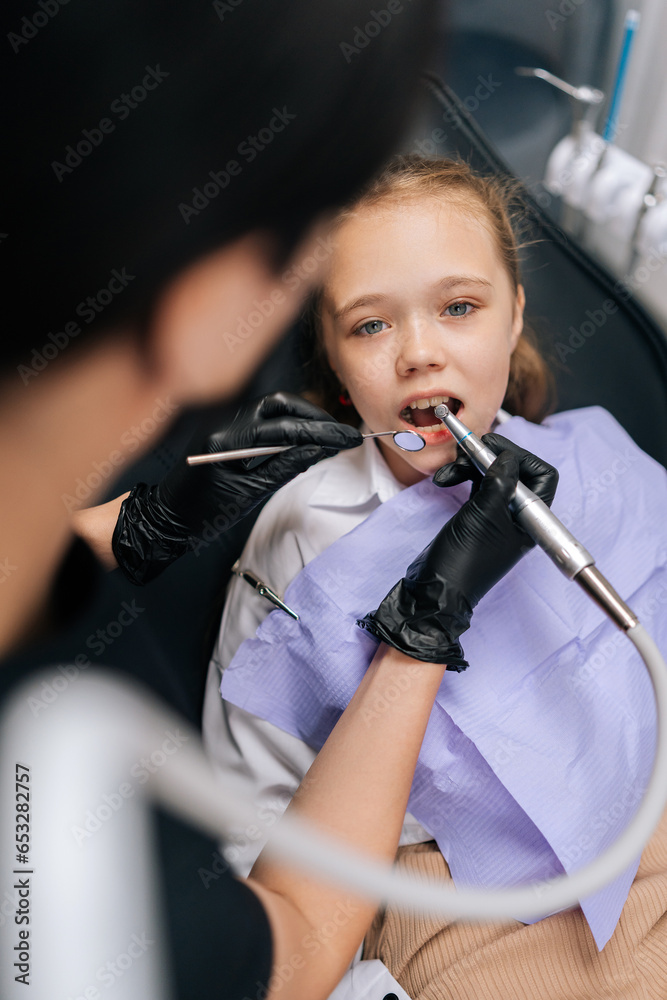 Vertical portrait of adorable little child girl sitting in stomatology seat with open mouth ...