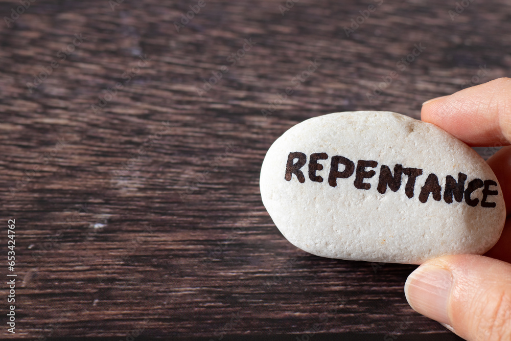 Hand-holding rock with handwritten word "repentance" over a wooden ...