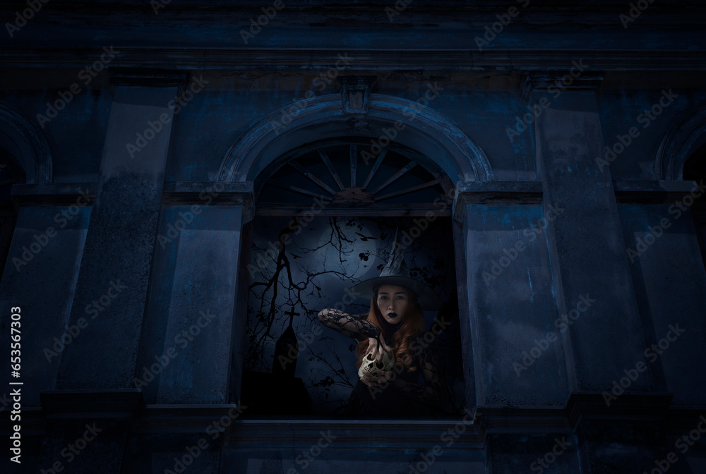 Halloween witch holding a skull standing in old damaged window with ...
