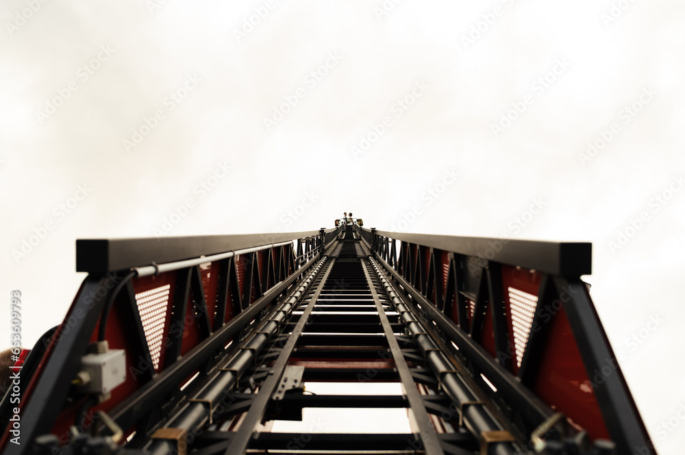 Tall extendable fire ladder close up in perspective on cloud sky ...