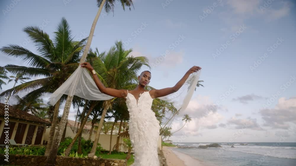 Androgynous black bride posing in wedding dress. Wind blows airy veil in air. Gender fluid ...