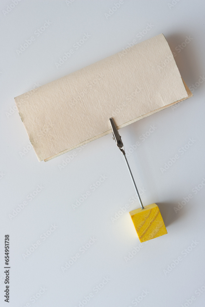 folded paper and alligator clip with yellow cube base on plain paper ...