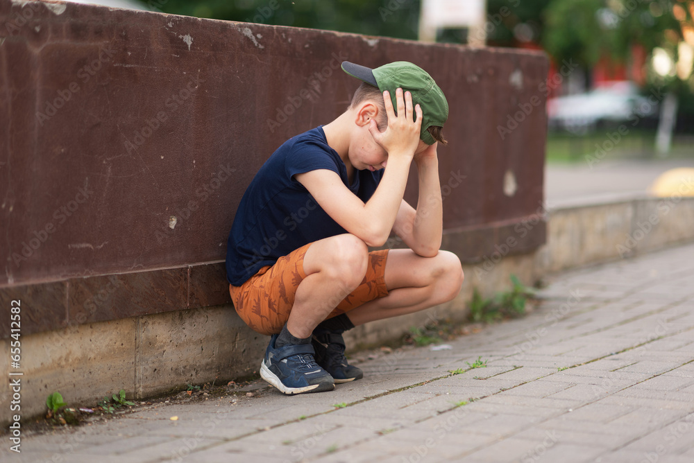 A teenage boy is squatting leaning against a concrete wall on the ...