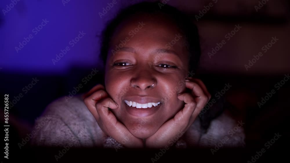 Close up of young black girl laughing and watching screen at home at ...