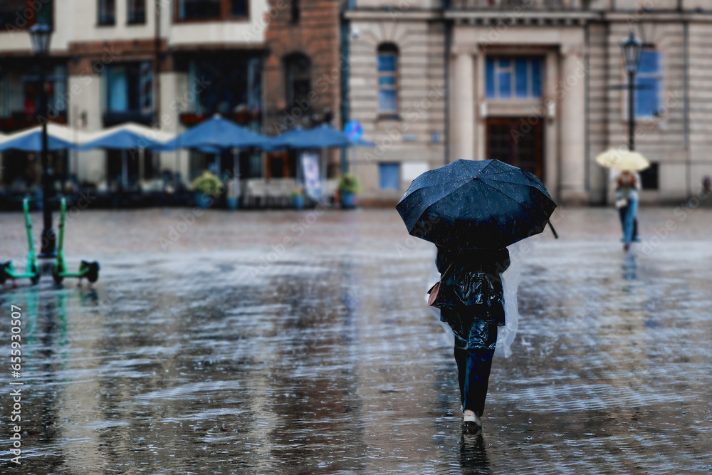 A woman walks down the street with an umbrella in bad rainy weather ...