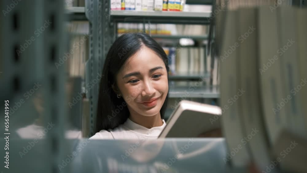 Pretty girl chooses books, standing in public library. Asian female ...