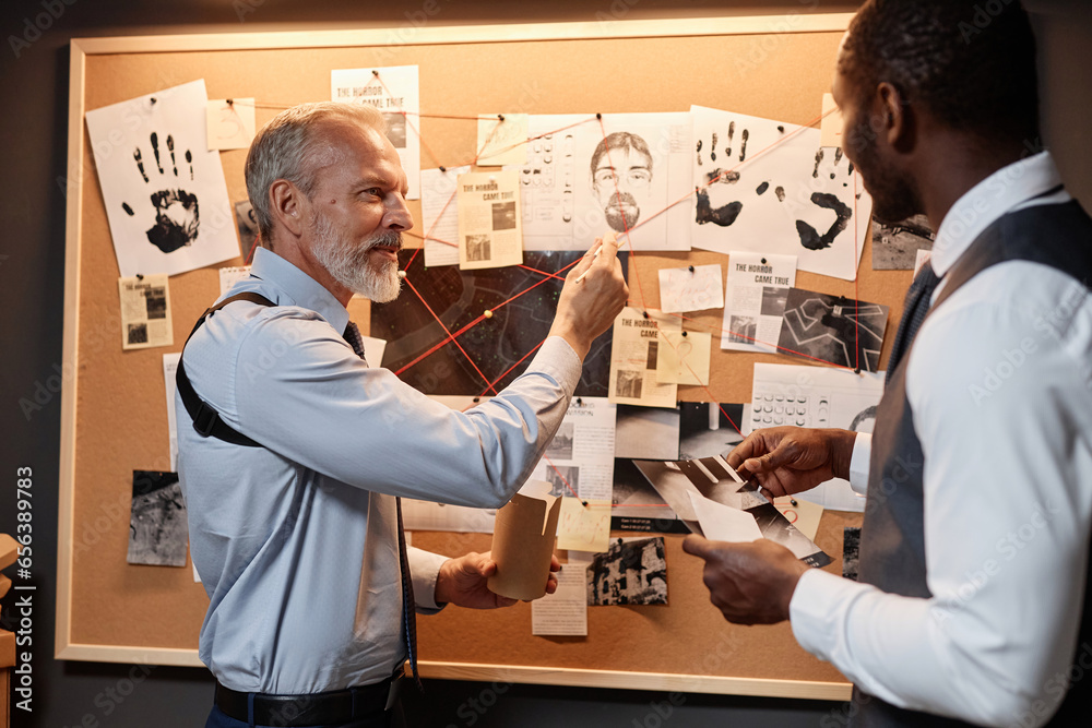 Side view portrait of two detectives pointing at evidence board while ...