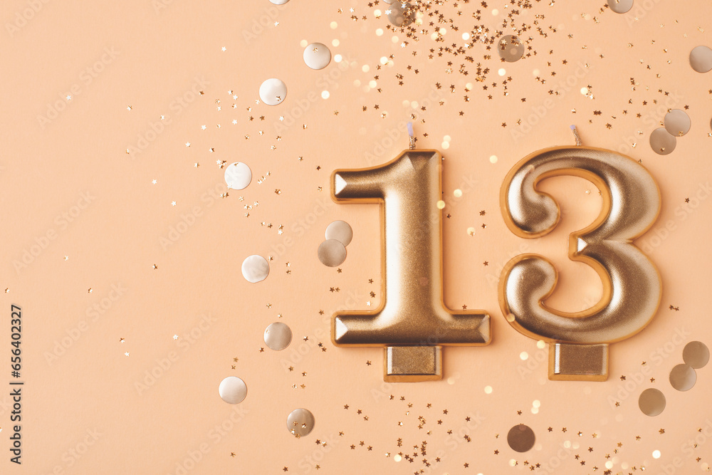 Gold candles in the form of number thirteen on peach background with ...
