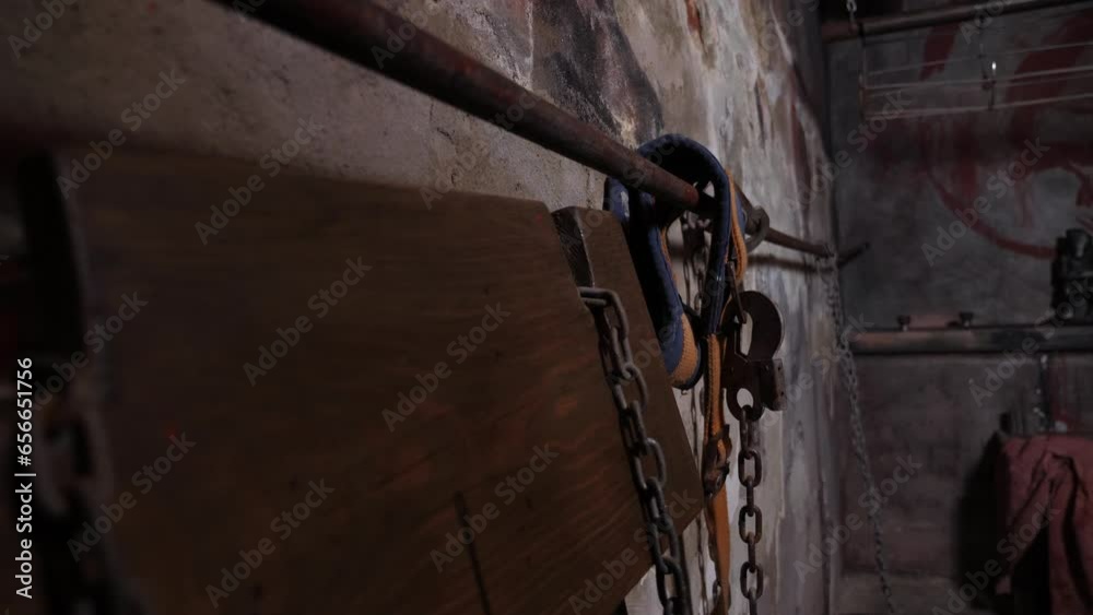 Close-up of an old rusty chain with handcuffs hanging on the gray dirty wall of the prison ...