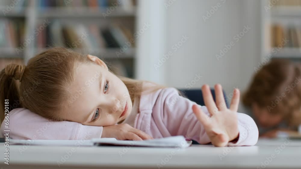 Close up of bored little girl lying on desk at classroom and tapping ...