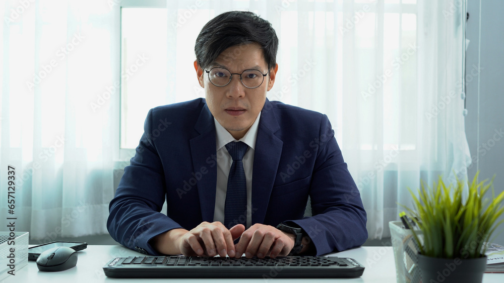 serious asian business man in suit using computer on desk looking ...