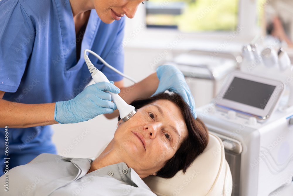 Elderly woman undergoing device-driven cosmetic facial treatment using ...