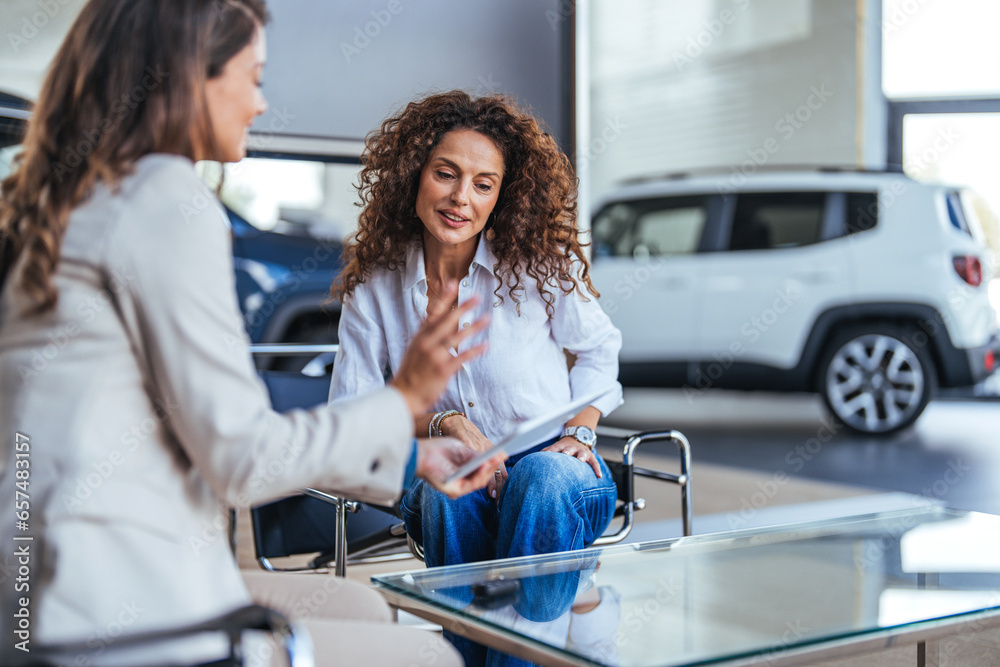 Saleswoman and a female customer in a car dealership. Sales manager ...