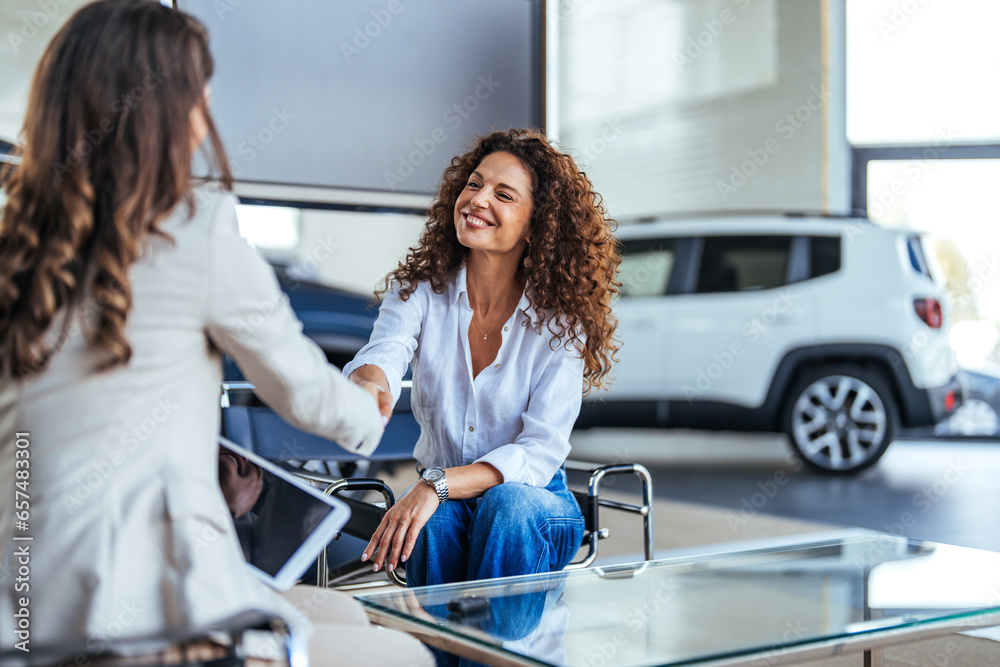 Smiling car saleswoman discussing a contract with a female customer ...