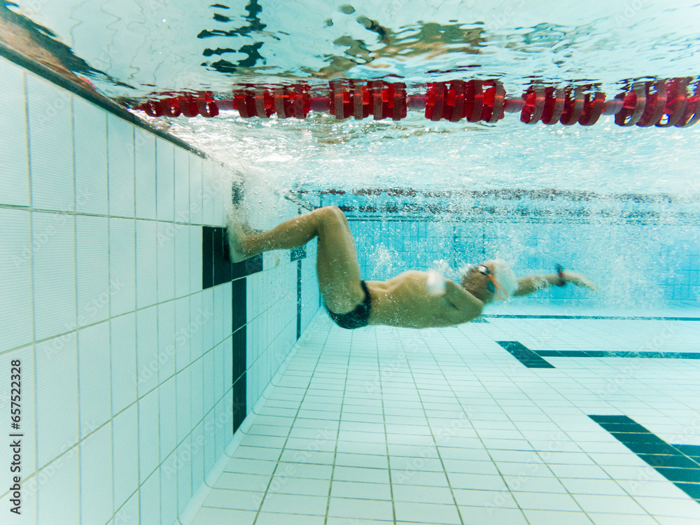 An adult man with an amputated arm is swimming underwater in a heated ...