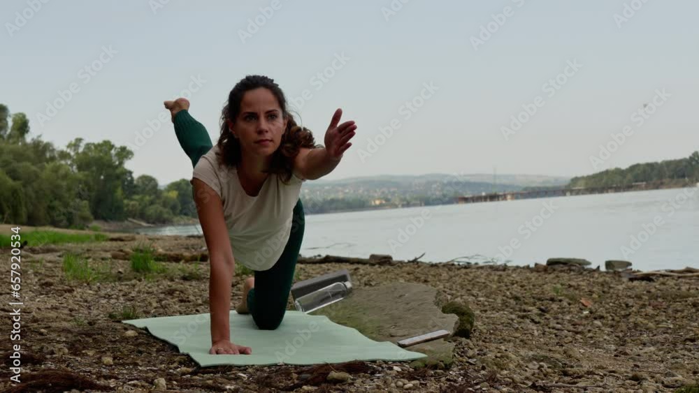 Vidéo Stock A Caucasian girl on a mat by the river, doing stretching ...