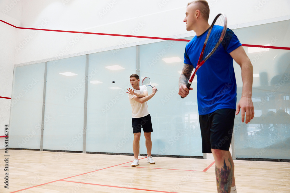Two young men, friends playing squash together on squash court ...