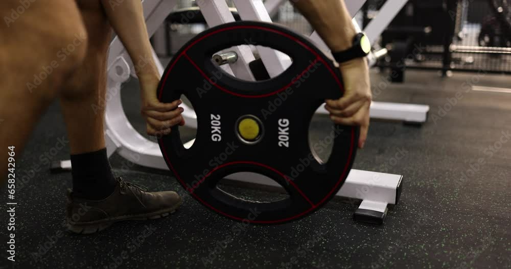 Athlete places barbell disc on rack in gym weighing 20 kg. Barbell ...