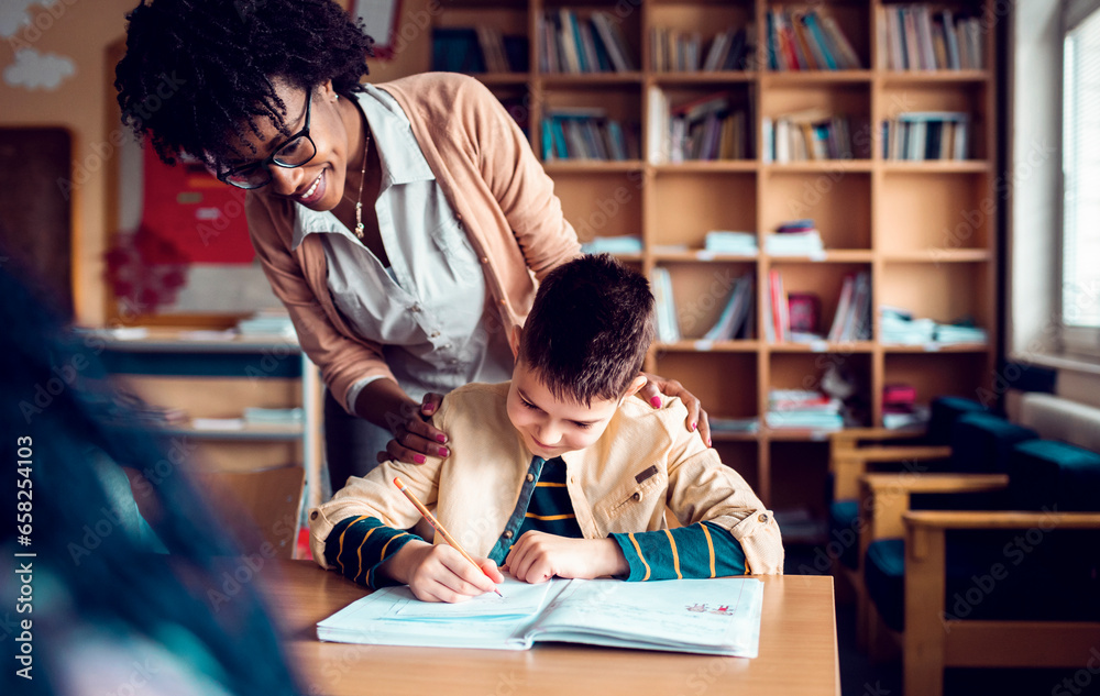 Young Caucasian boy asking for help from his teacher while at the ...
