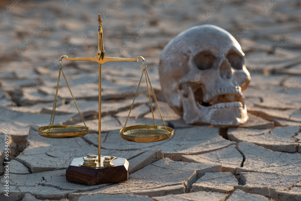 Scales of justice and a human skull on heat-cracked clay in the desert ...