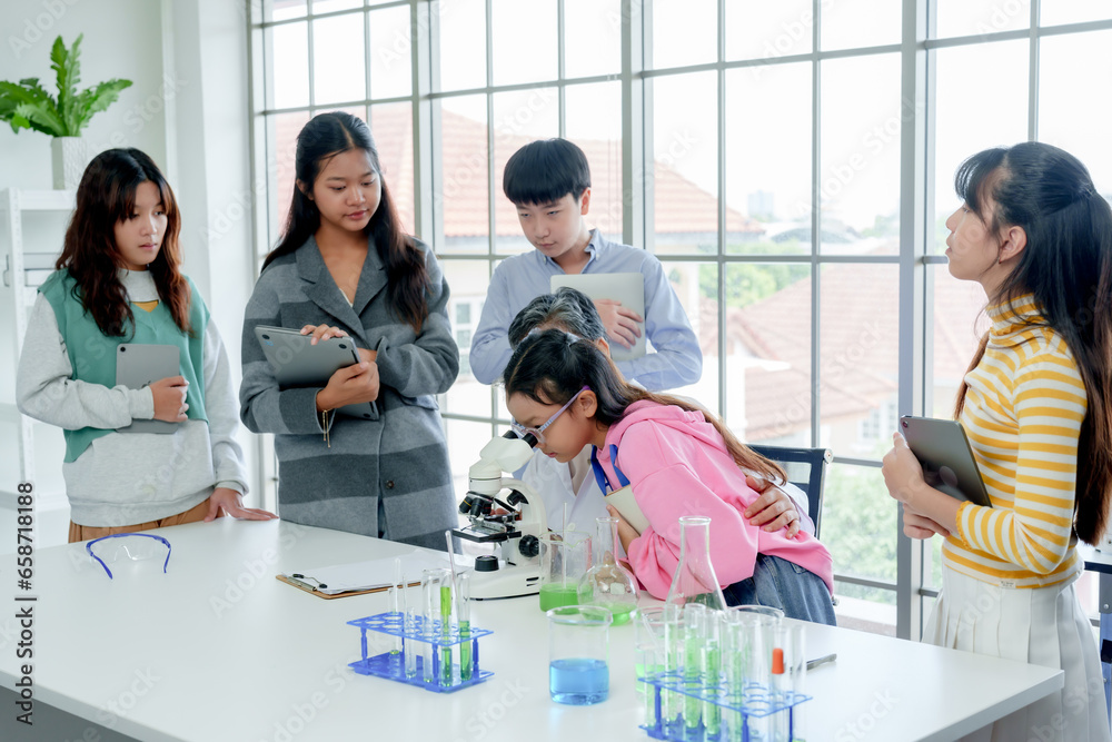 Schoolgirl and friends in classroom Trying out microscope during ...