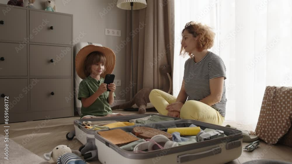 Mom and kid pack suitcase together for vacation. Serious boy leader ...